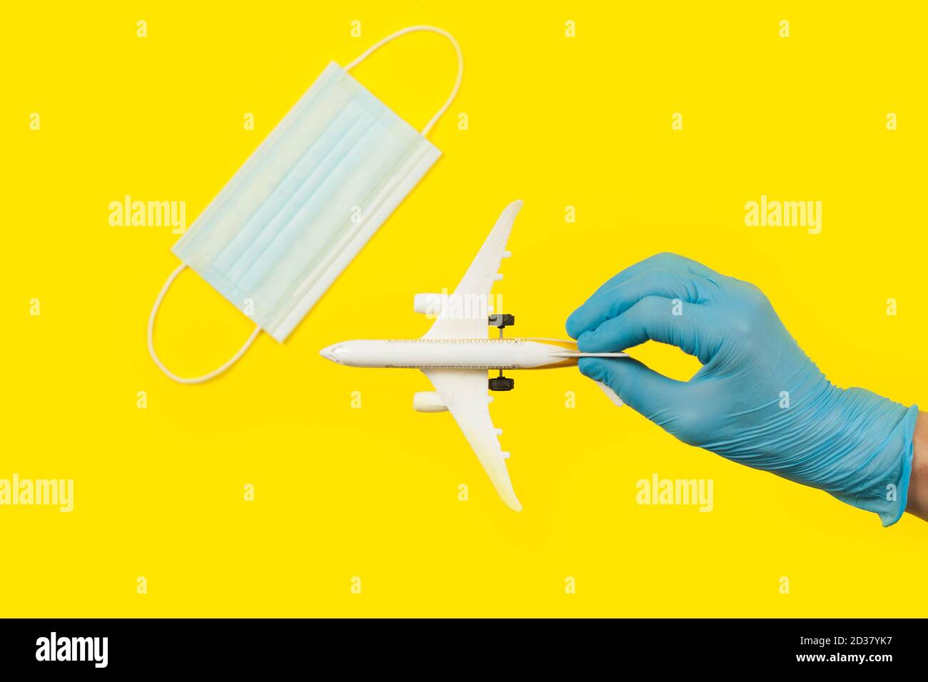 Hand in glove holding model airplane over face mask. Air travel resumes ...