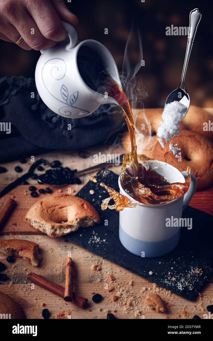 Mans hand serving a very hot coffee splash in ceramic cup with biscuits ...