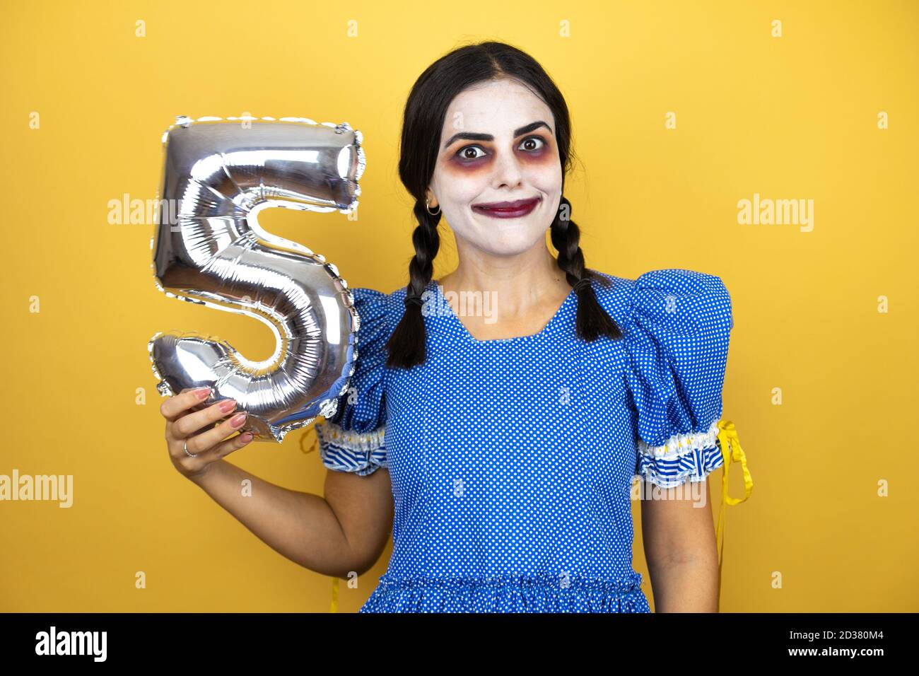 woman wearing a scary doll halloween costume over yellow background ...