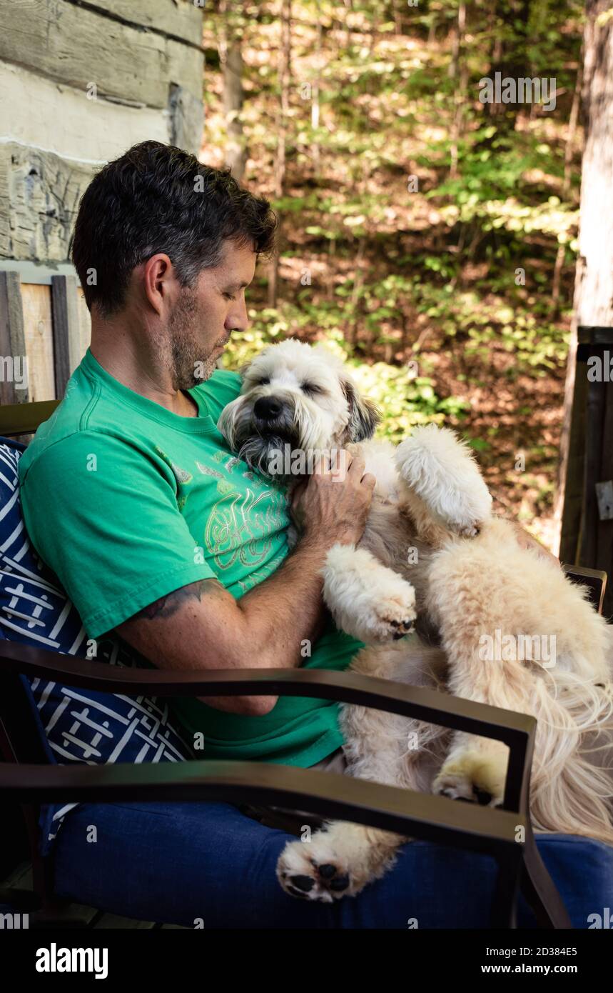 Man holding a fluffy dog on his lap outside on a deck in the woods ...