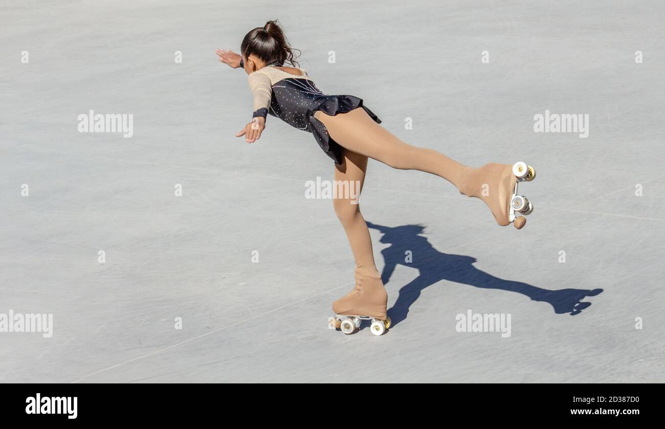 Teenage girl's back shot performing a figure skating on wheels. Pigeon ...