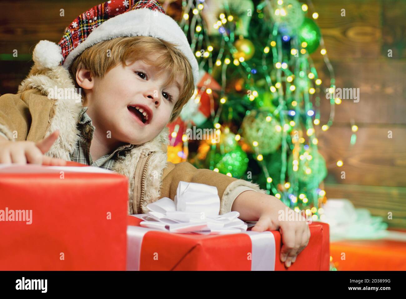 Winter kid. Child with a Christmas present on wooden house background ...