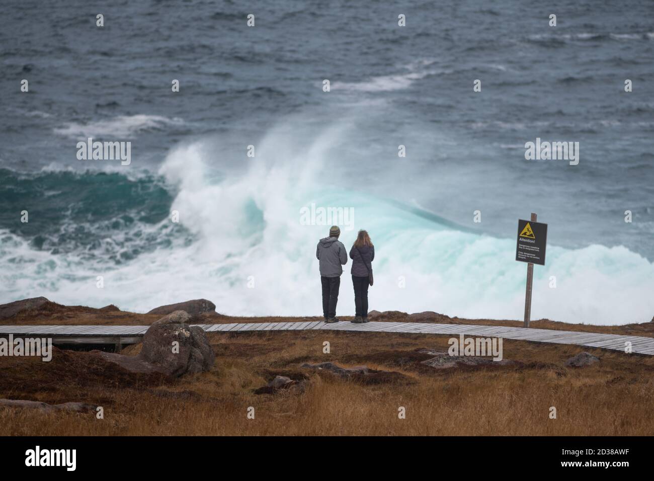 Two people stand at the ocean's edge watching large waves rolling in ...