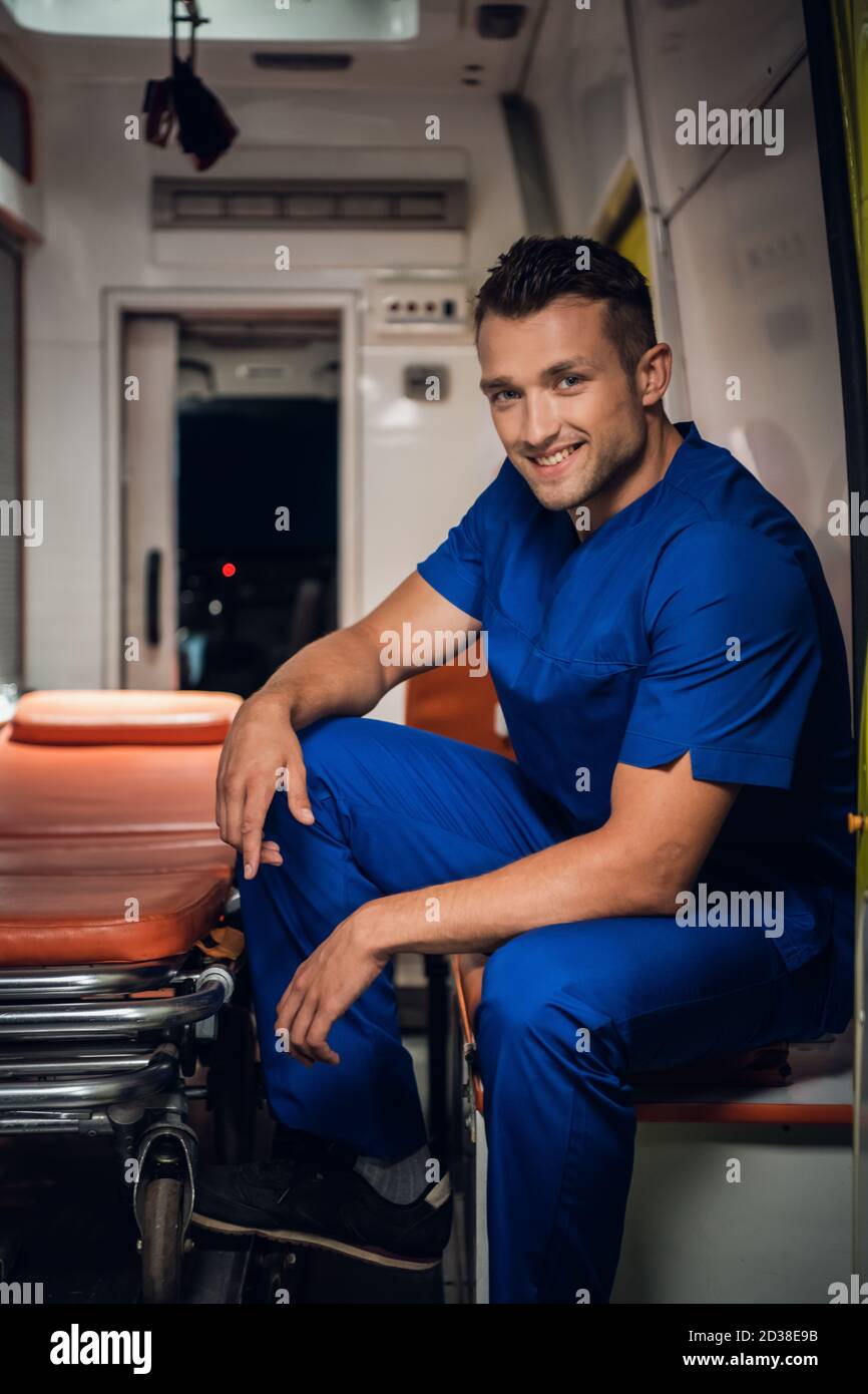 A portrait of a smiling paramedic in a uniform sitting in the back of ...
