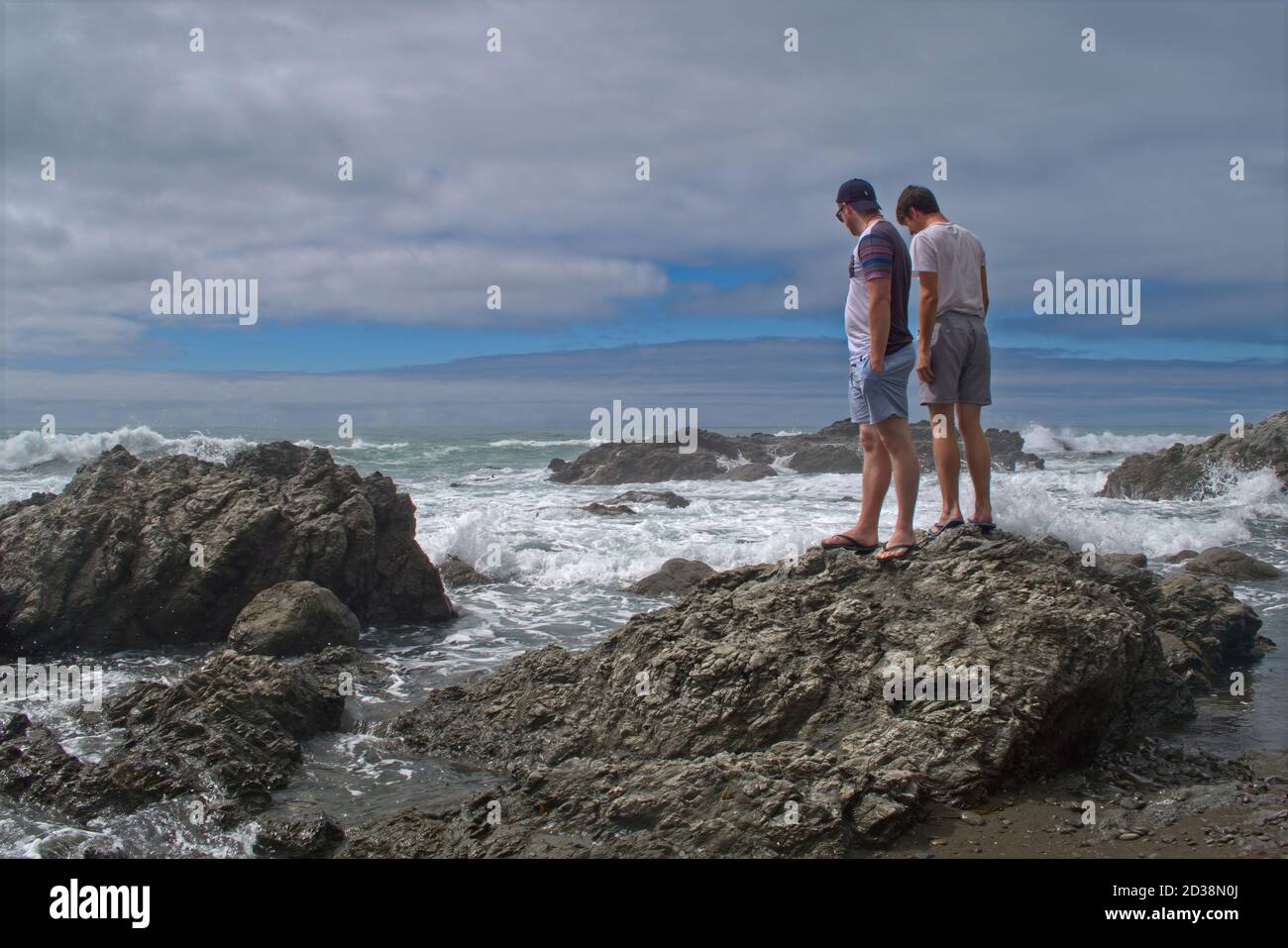 Two Young Men Standing on Rocks Watching the Surf Stock Photo - Alamy