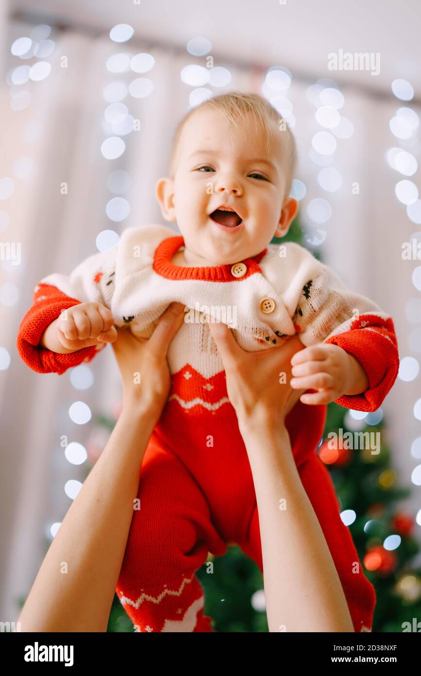 Baby in a knitted Christmas onesie in her mother's arms in front of a ...
