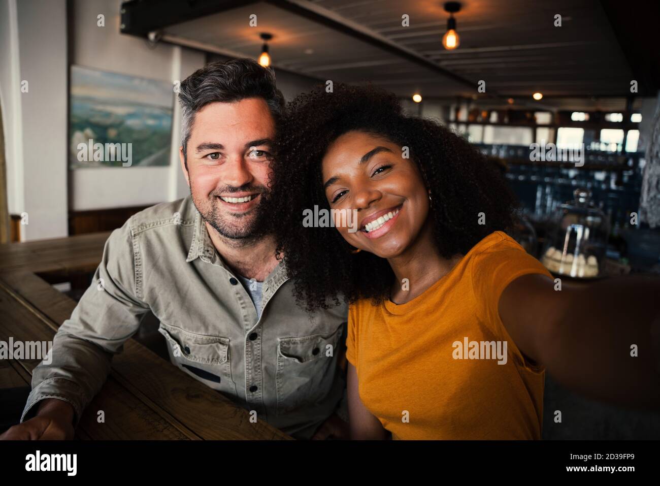 multi race couple smiling happily into camera in bright coffee shop ...