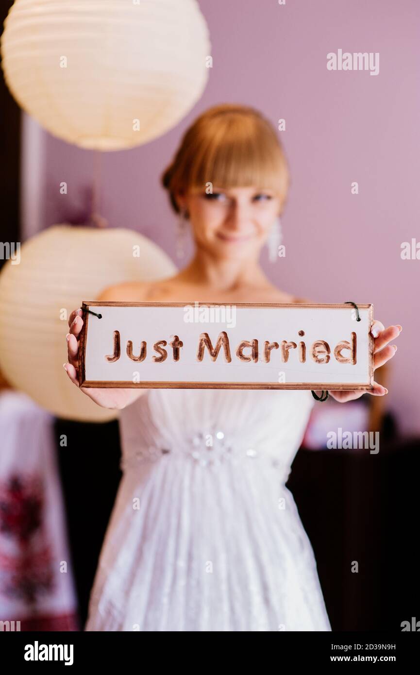Young blonde bride on her wedding day holds a wooden board with the ...