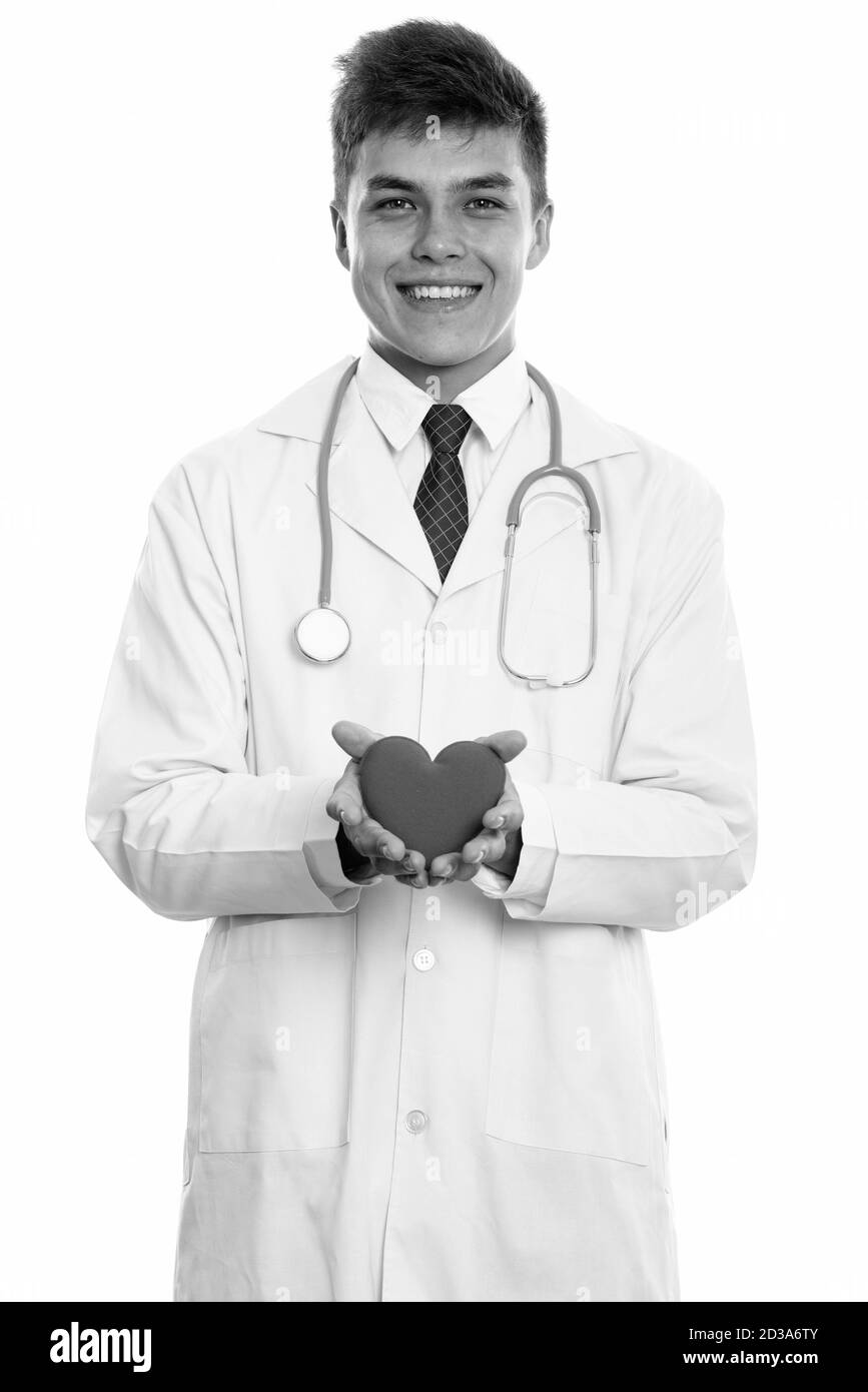 Studio shot of young happy man doctor smiling while holding red heart ...