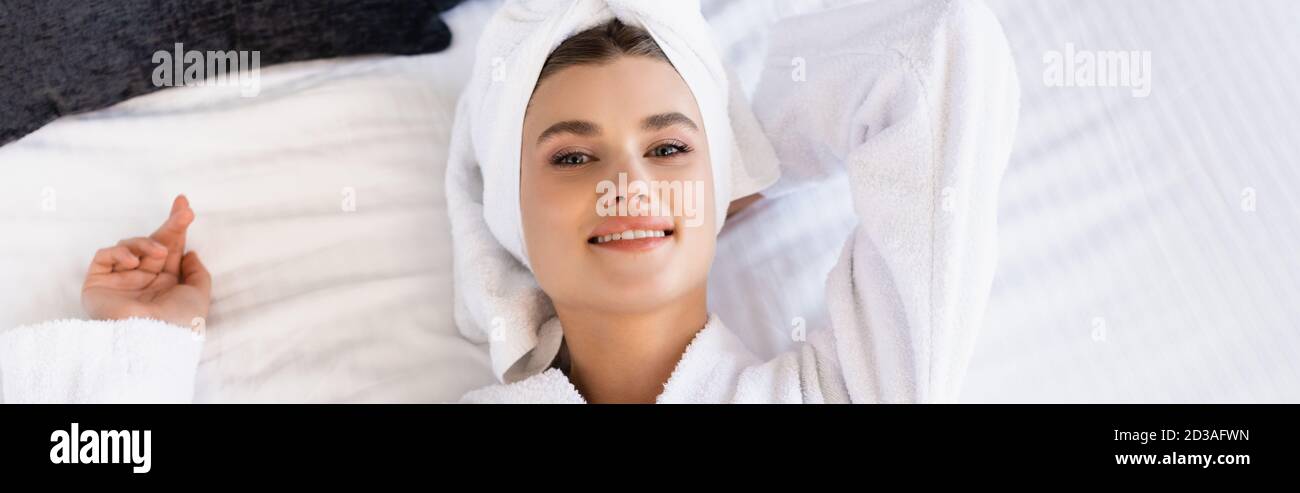 top view joyful woman in towel and white bathrobe lying on bed in hotel ...