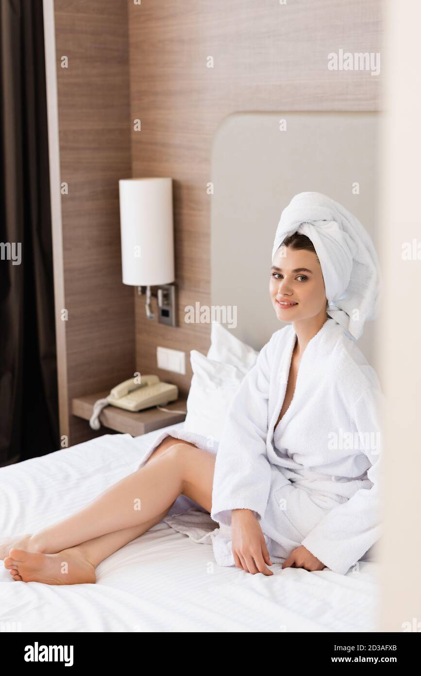 pleased and barefoot woman in towel and white bathrobe lying on bed in ...