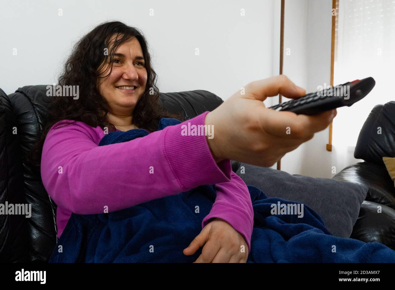 Happy woman holding the remote control for the TV Stock Photo - Alamy