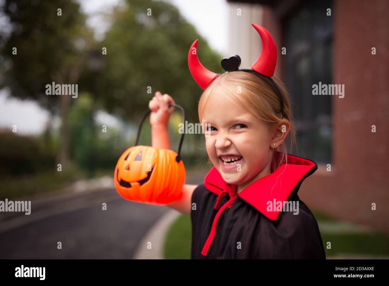 Little Girl in costume of devil with red horns in park. Happy Halloween ...
