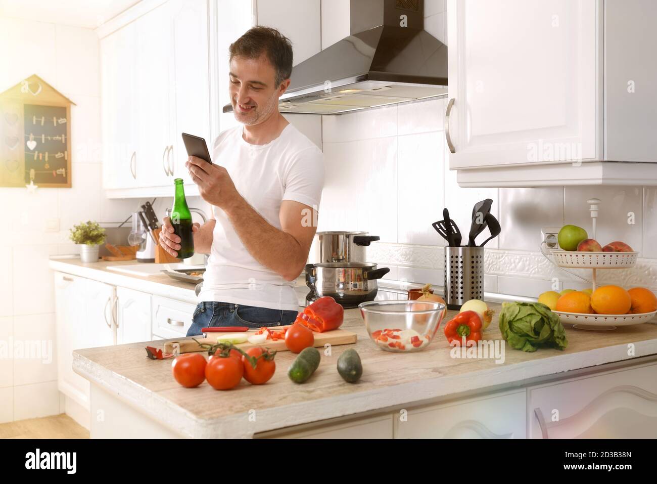 Happy man in the kitchen looking at a cell phone and having a beer ...