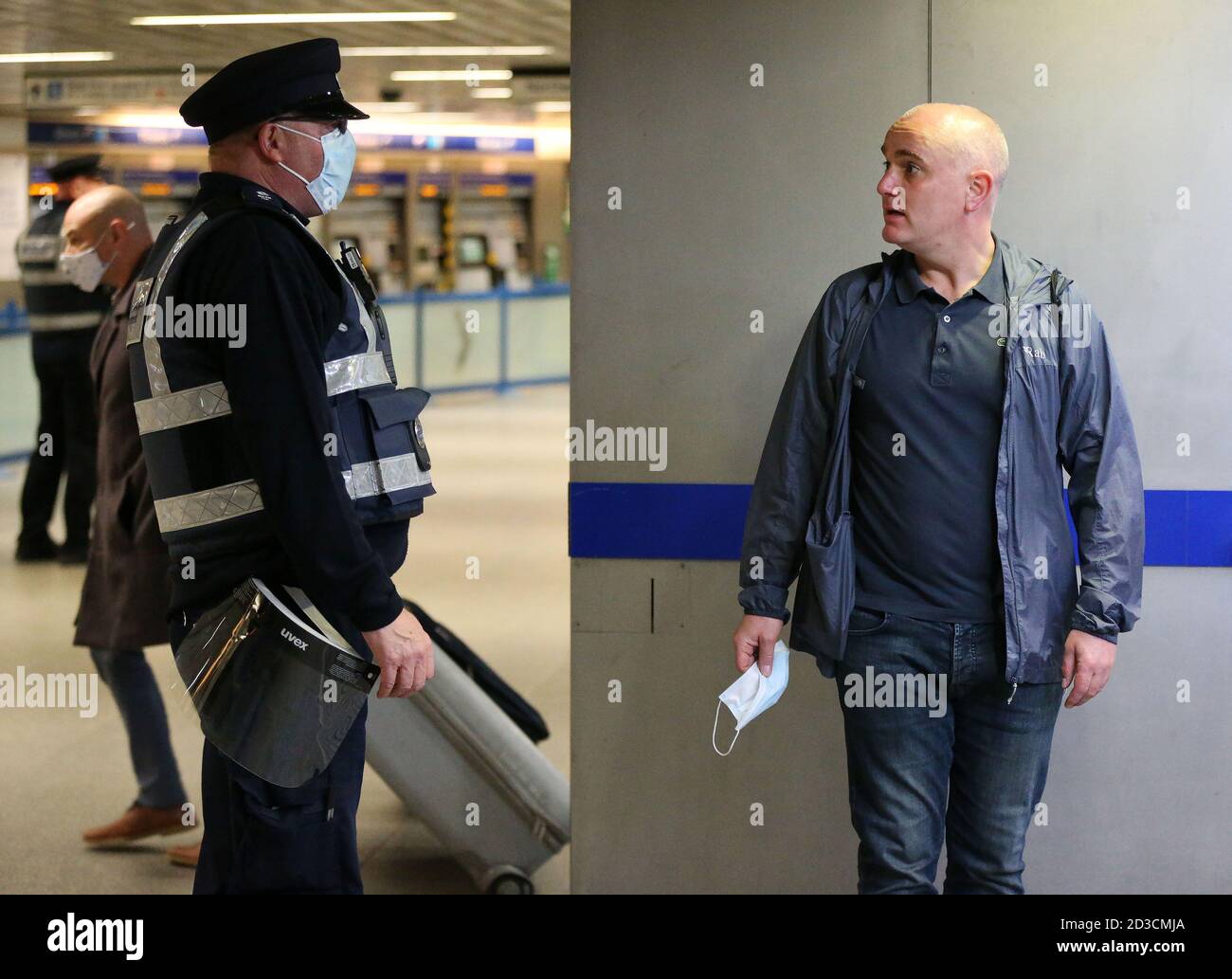 A man holds his face mask in his hand while being spoken to by a TfL ...