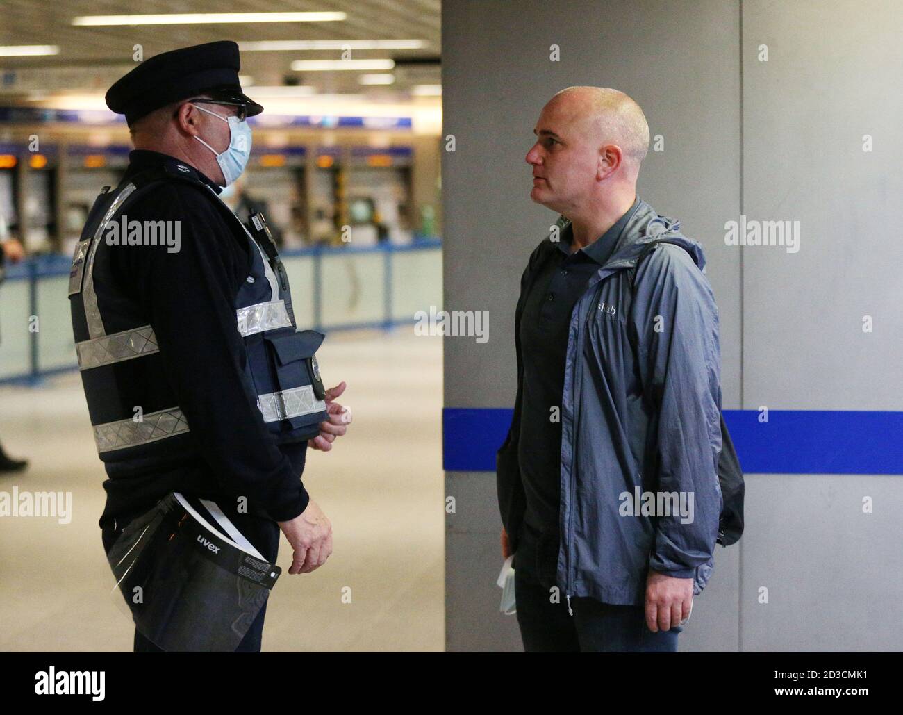 A man holds his face mask in his hand while being spoken to by a TfL ...
