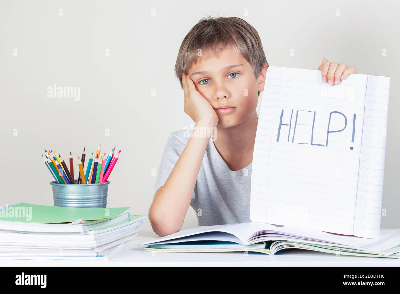 Sad tired boy doing homework and holding notebook with word Help Stock ...