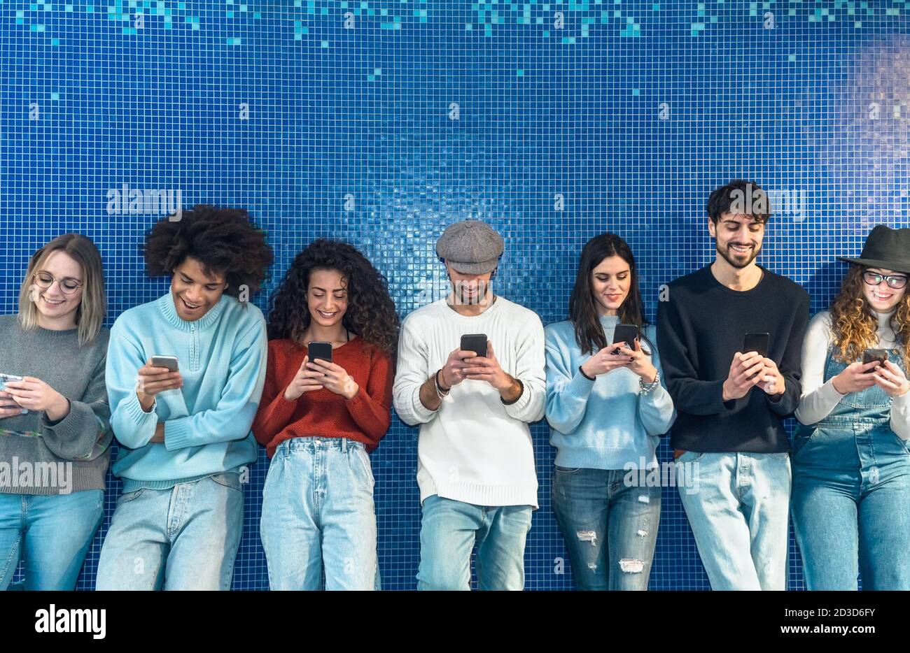 Young people using mobile smartphone while standing against blue ...