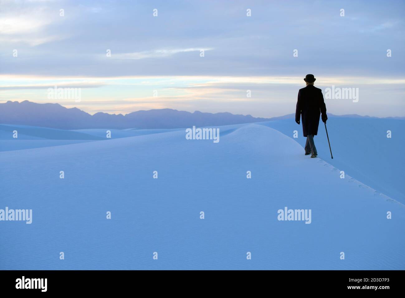 Rear view of man in a coat and bowler hat walking through a white dune ...