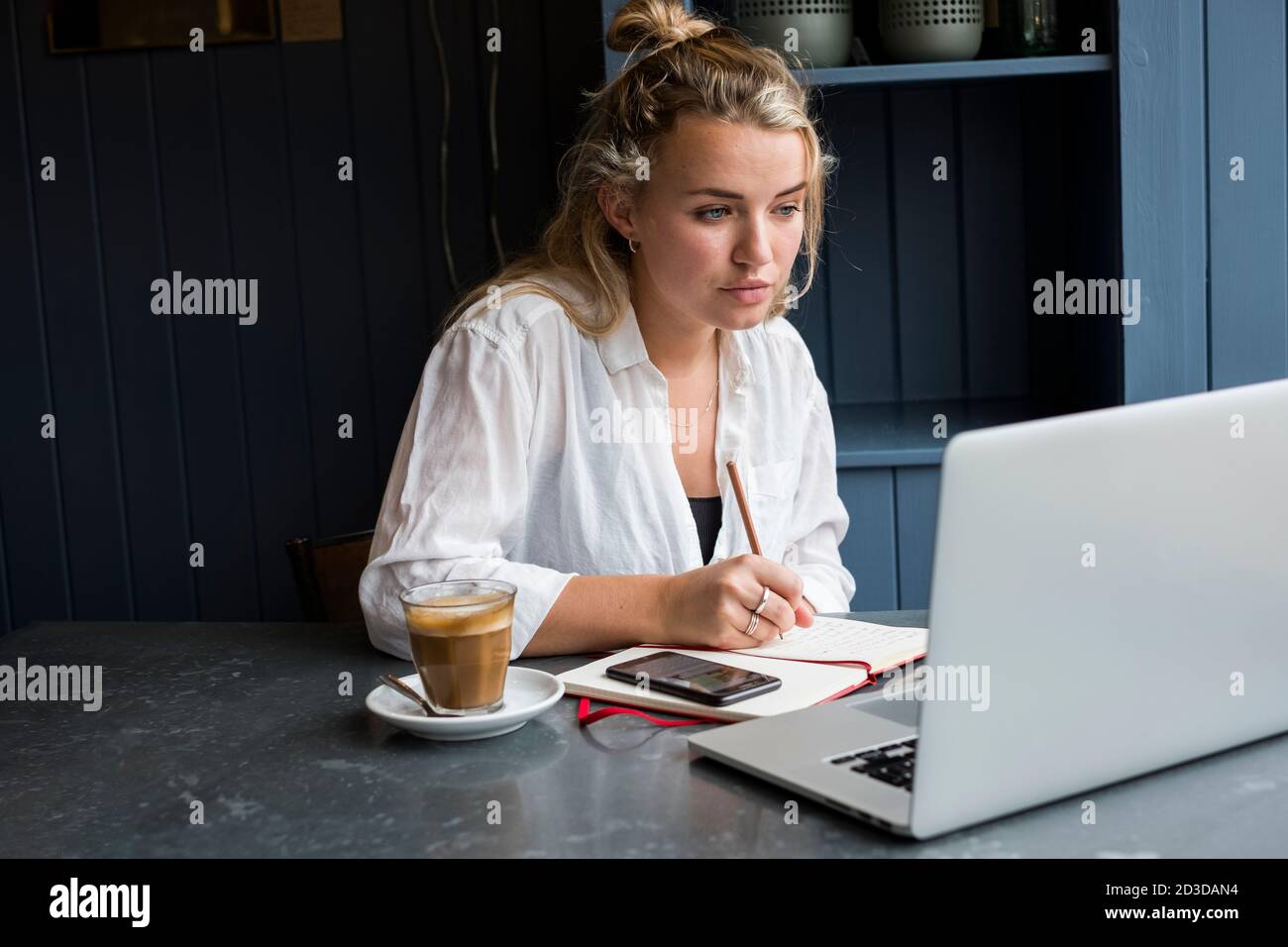 Woman sitting alone at a cafe table with a laptop , writing in note ...