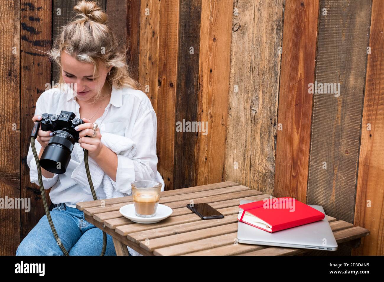 Young blond woman alone at an outdoor table, looking at digital camera ...