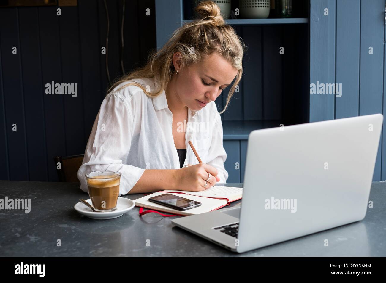Woman sitting alone at a cafe table with a laptop , writing in note ...