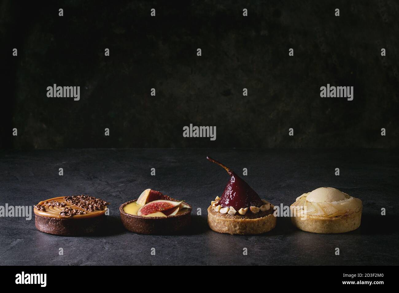 Variety of sweet tartlets with chocolate, caramel, pears, figs in row ...