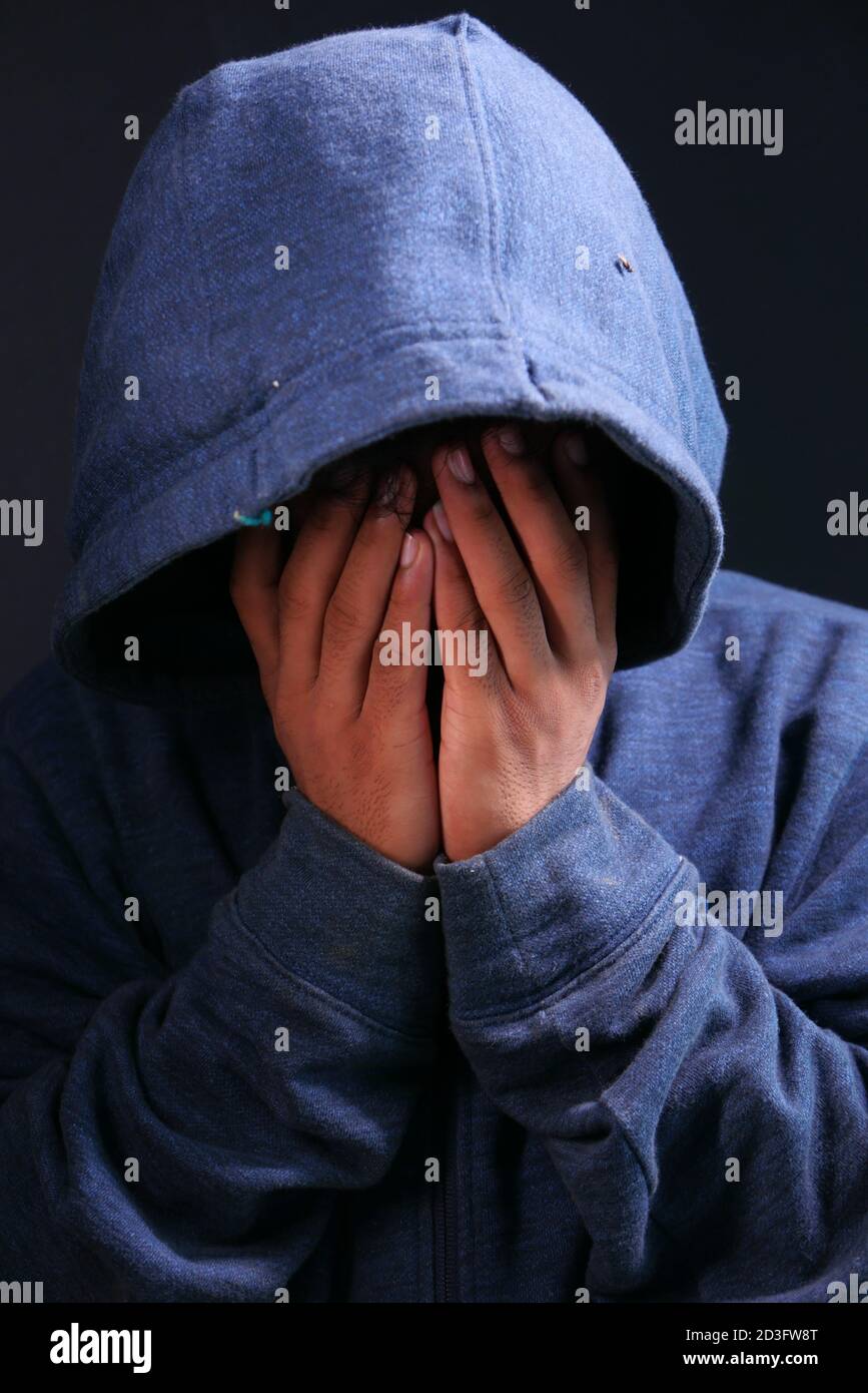 sad man in hood cover face with hands isolated in black Stock Photo - Alamy