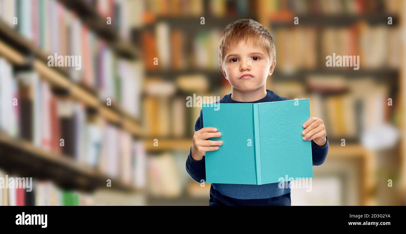 displeased little boy reading book over library Stock Photo - Alamy