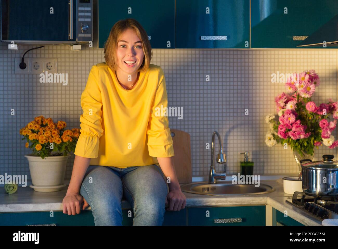 Housewife. Portrait of cute young woman sitting on kitchen countertops ...