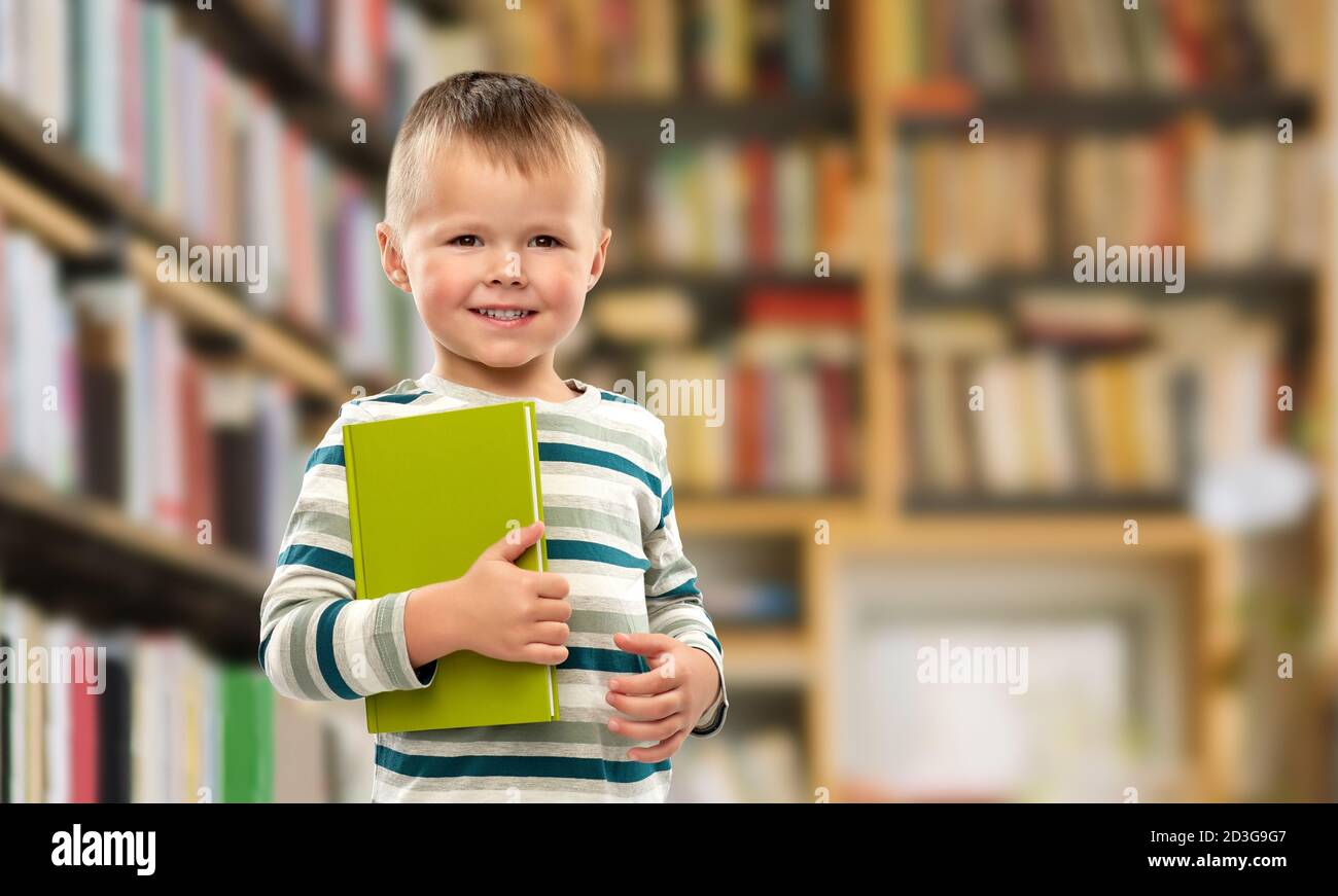 portrait of smiling boy holding book over library Stock Photo - Alamy
