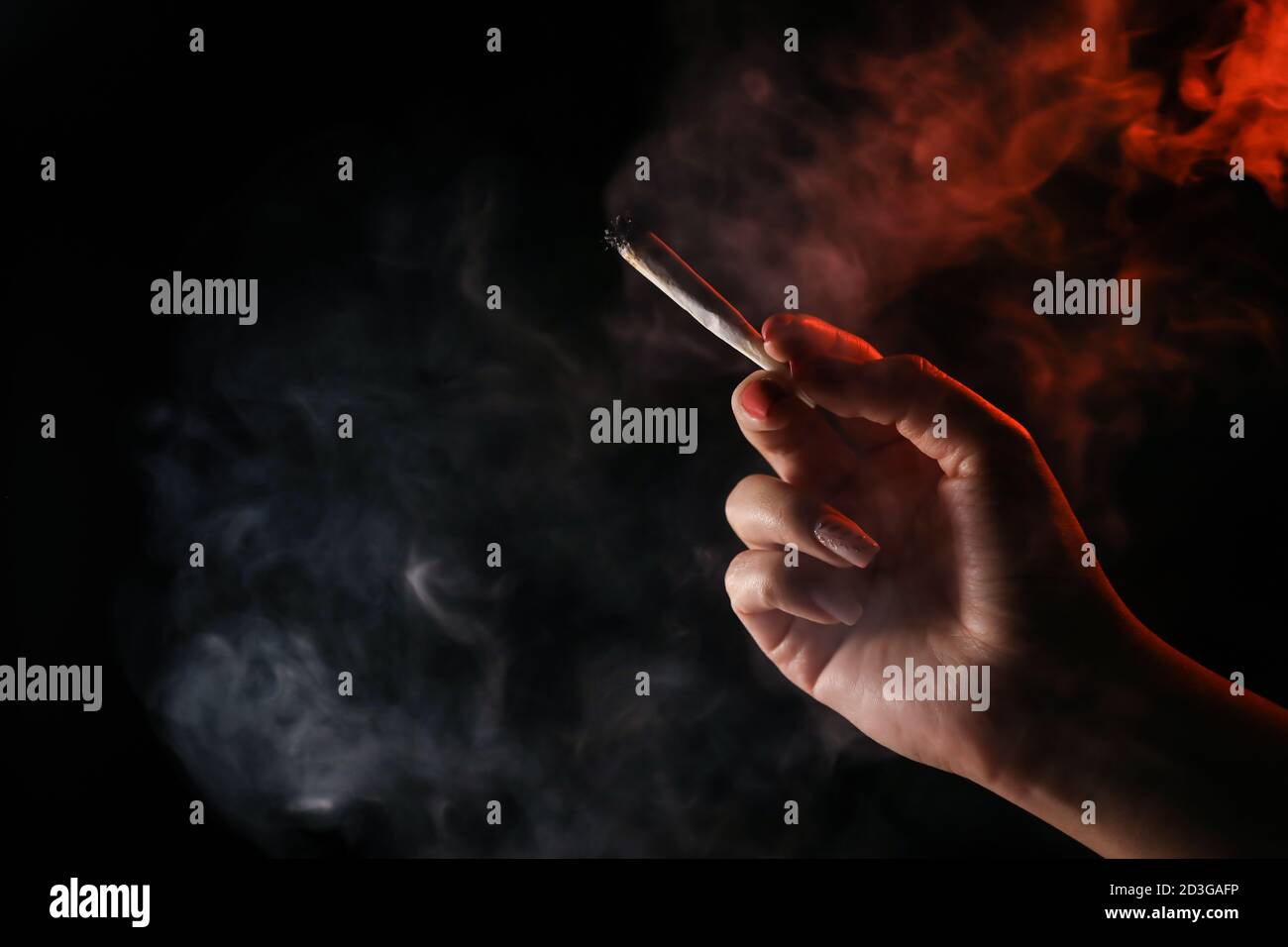 Woman hand holding cigarette in a smoke against black background ...