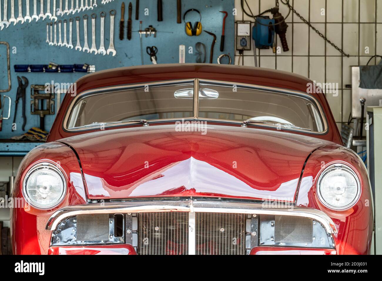 Red oldtimer car parked in a repair shop in front of a wall with screw ...