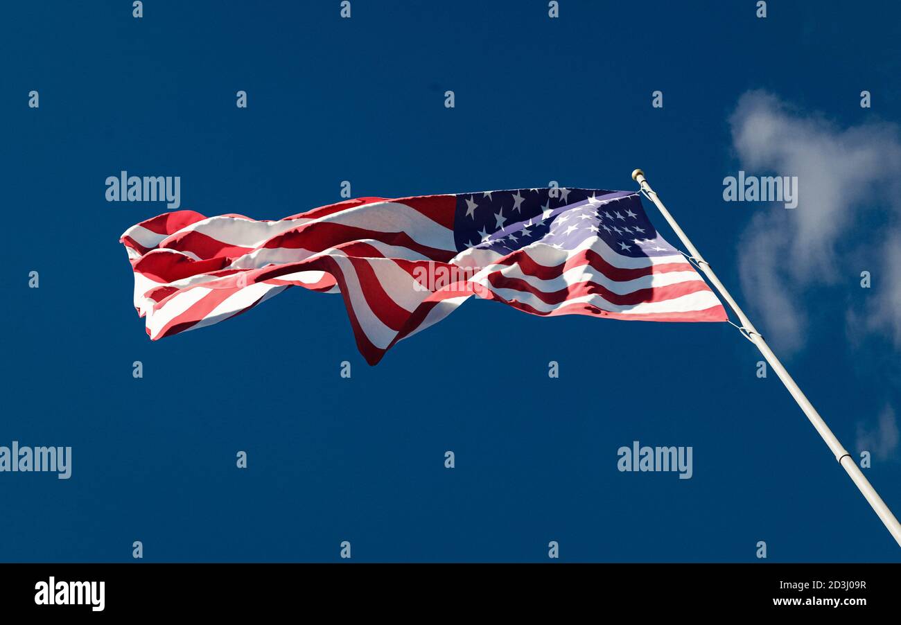 US national flag waving in the wind against a blue sky background low angle close up. Stars and ...