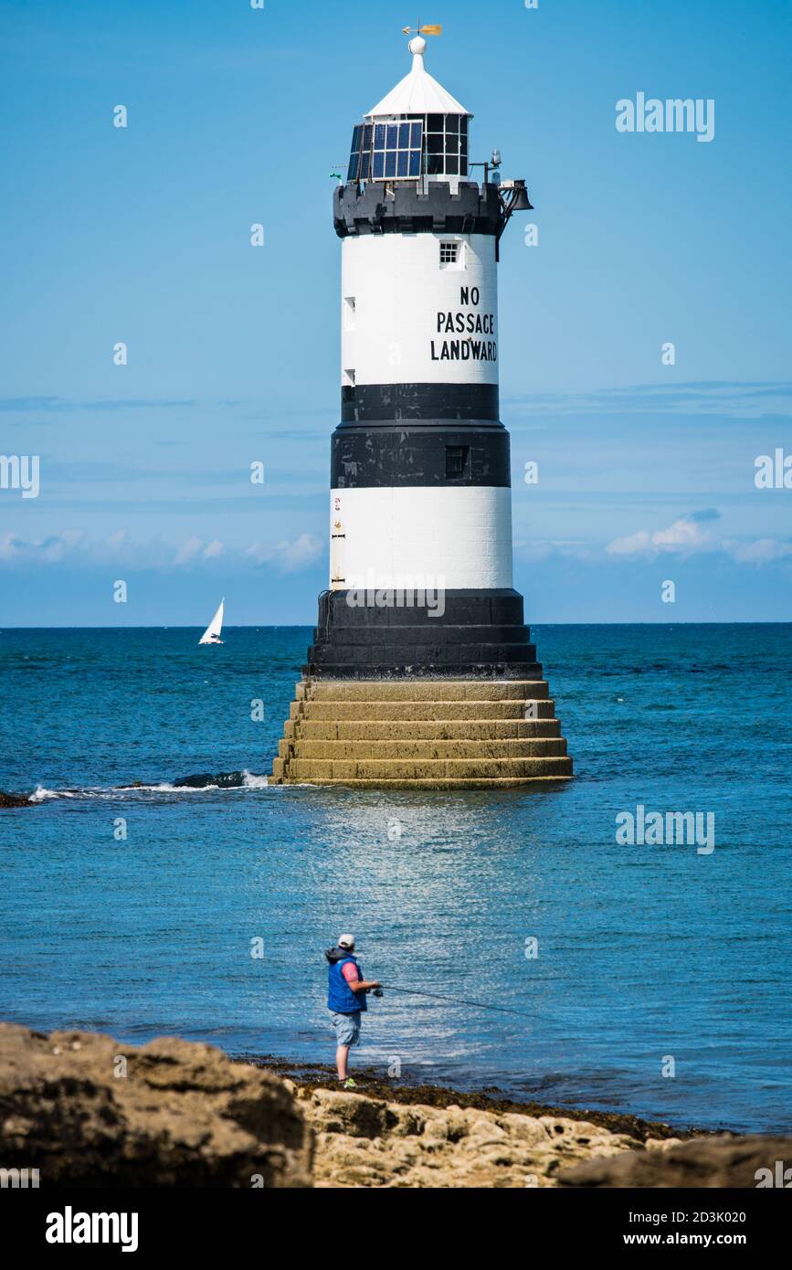 An angler fishes in the Irish Sea overlooked by the Trwyn Du Lighthouse ...