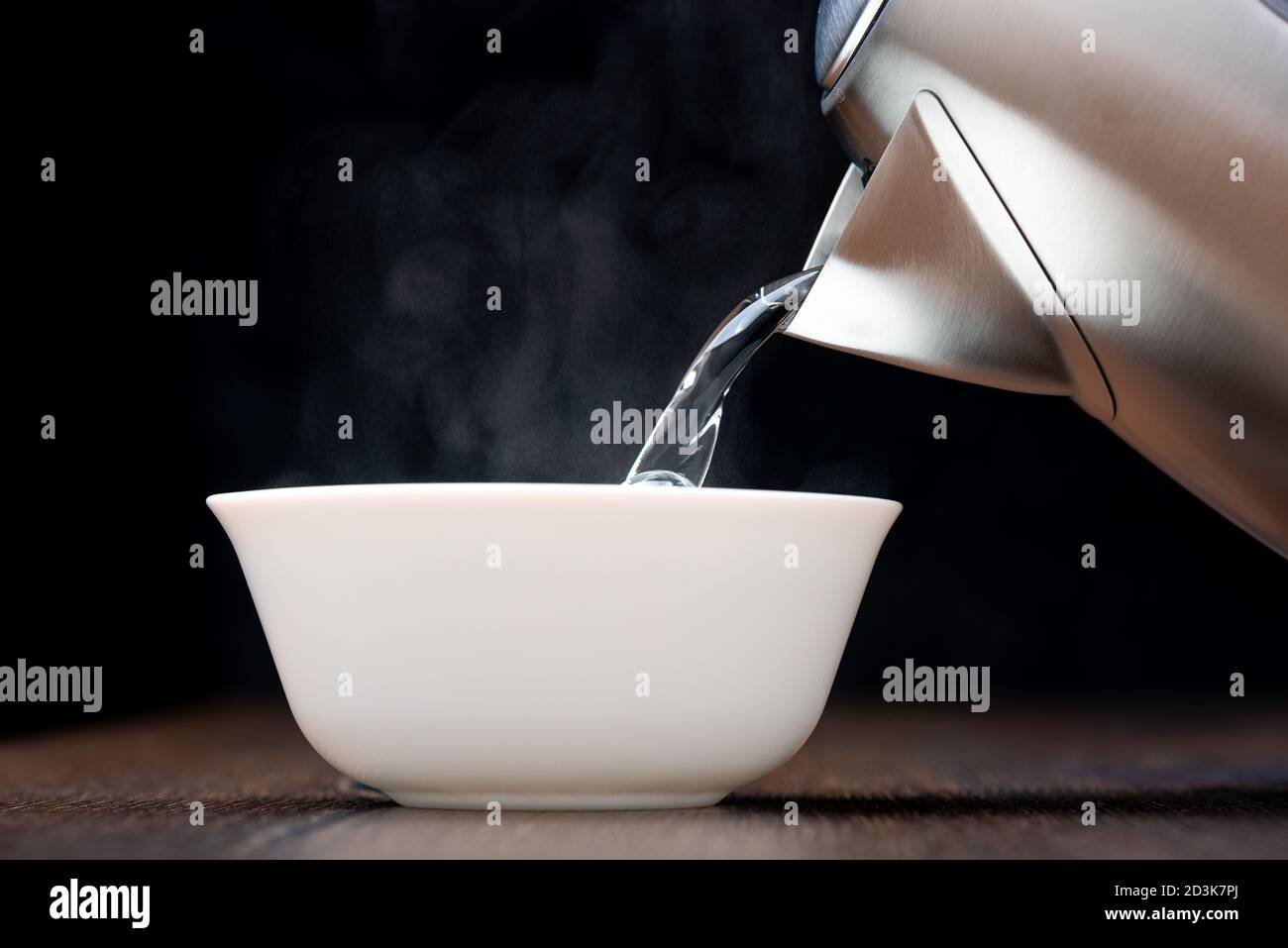 Pouring hot boiling water into a white bowl. Steam on a dark background Stock Photo - Alamy