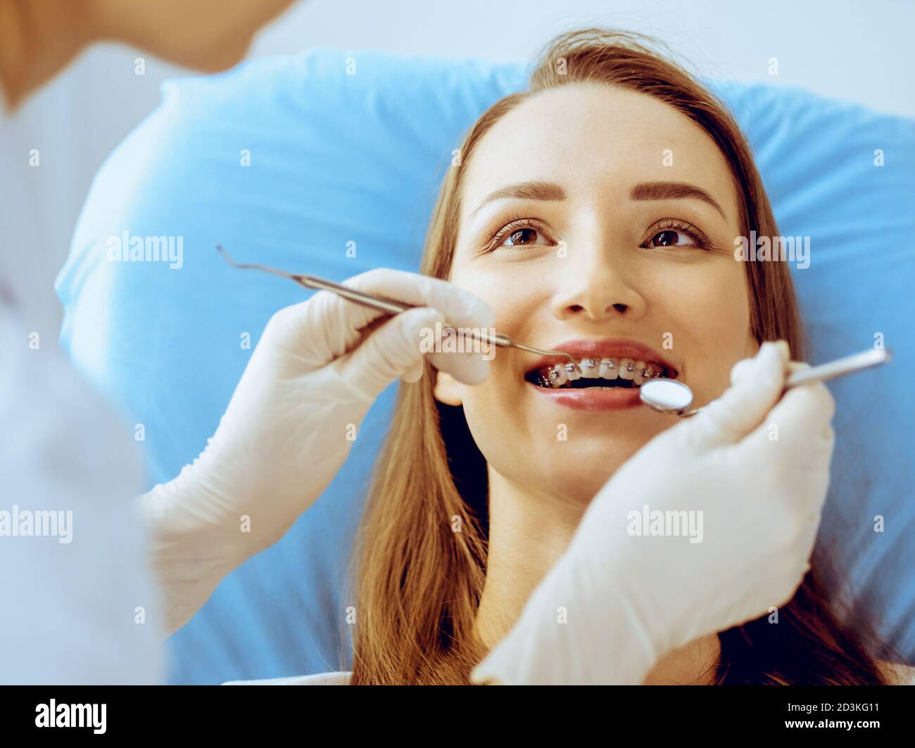Smiling young woman with orthodontic brackets examined by dentist in ...