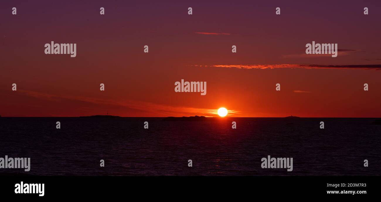 The sun setting in the ocean with small islands and a lighthouse in the ...