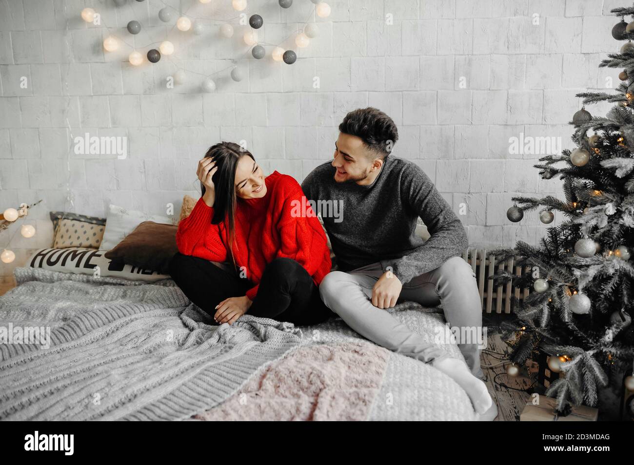 Cheerful couple in winter sweaters having fun lying on cozy bed and ...