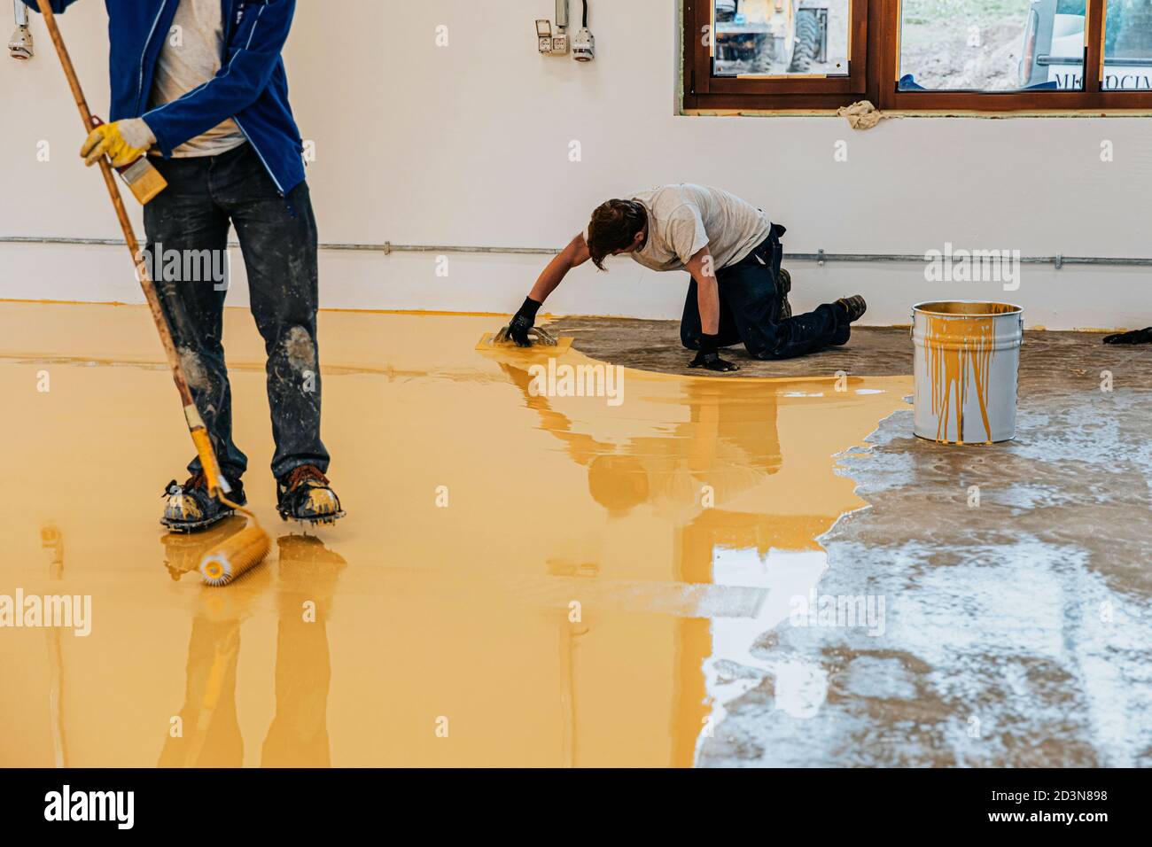 Worker, coating floor with self-leveling epoxy resin in industrial ...