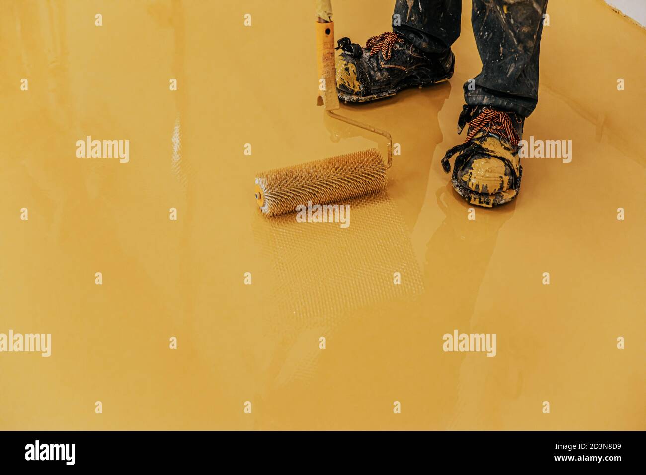 Worker, coating floor with self-leveling epoxy resin in industrial ...