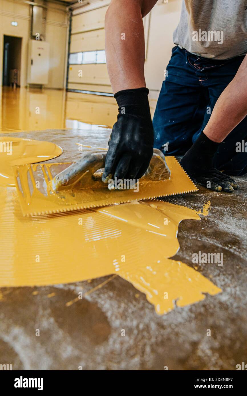 Worker, coating floor with self-leveling epoxy resin in industrial ...