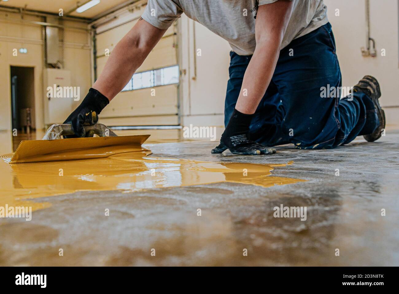 Worker, coating floor with self-leveling epoxy resin in industrial ...