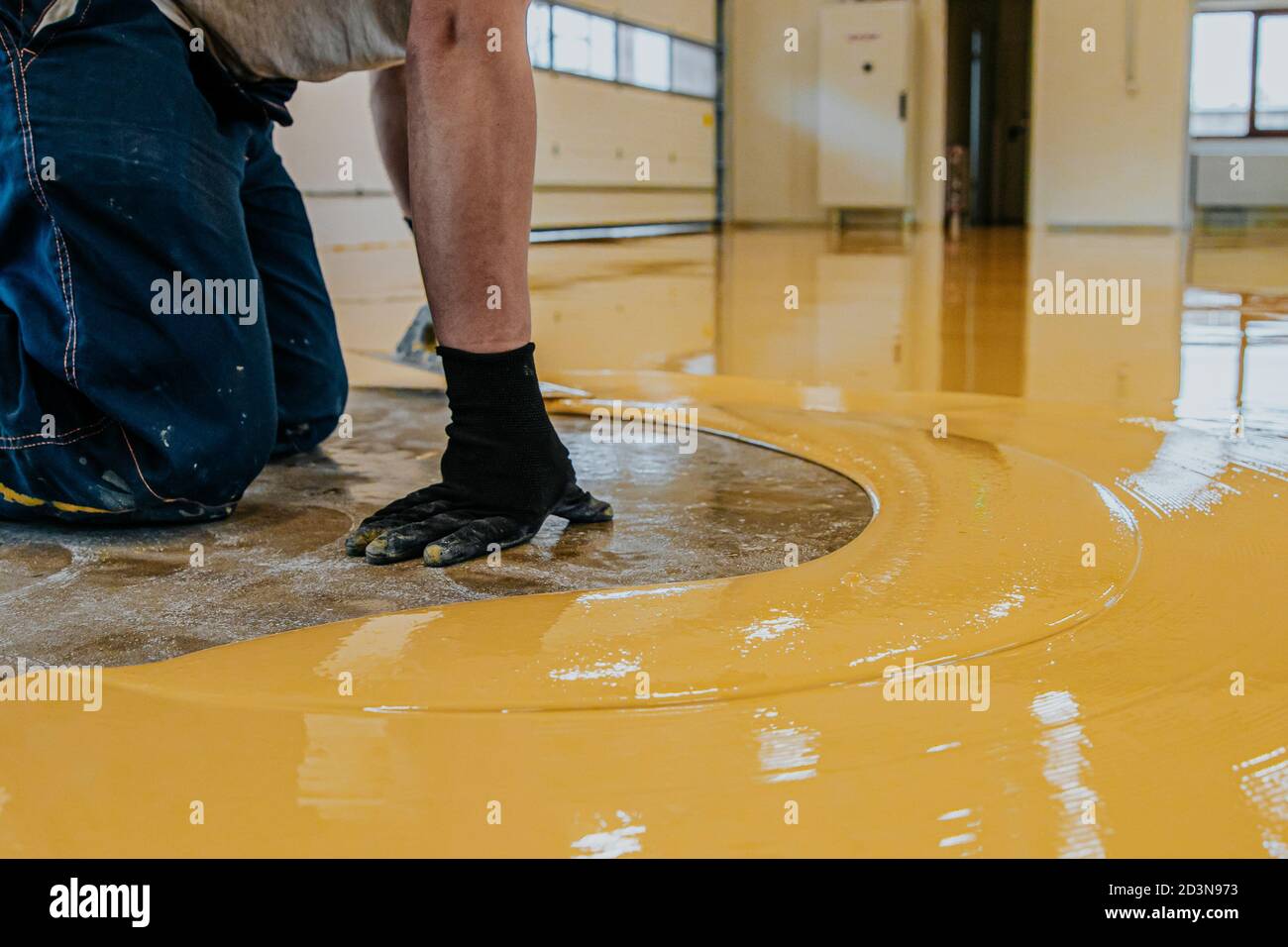 Worker, coating floor with self-leveling epoxy resin in industrial ...