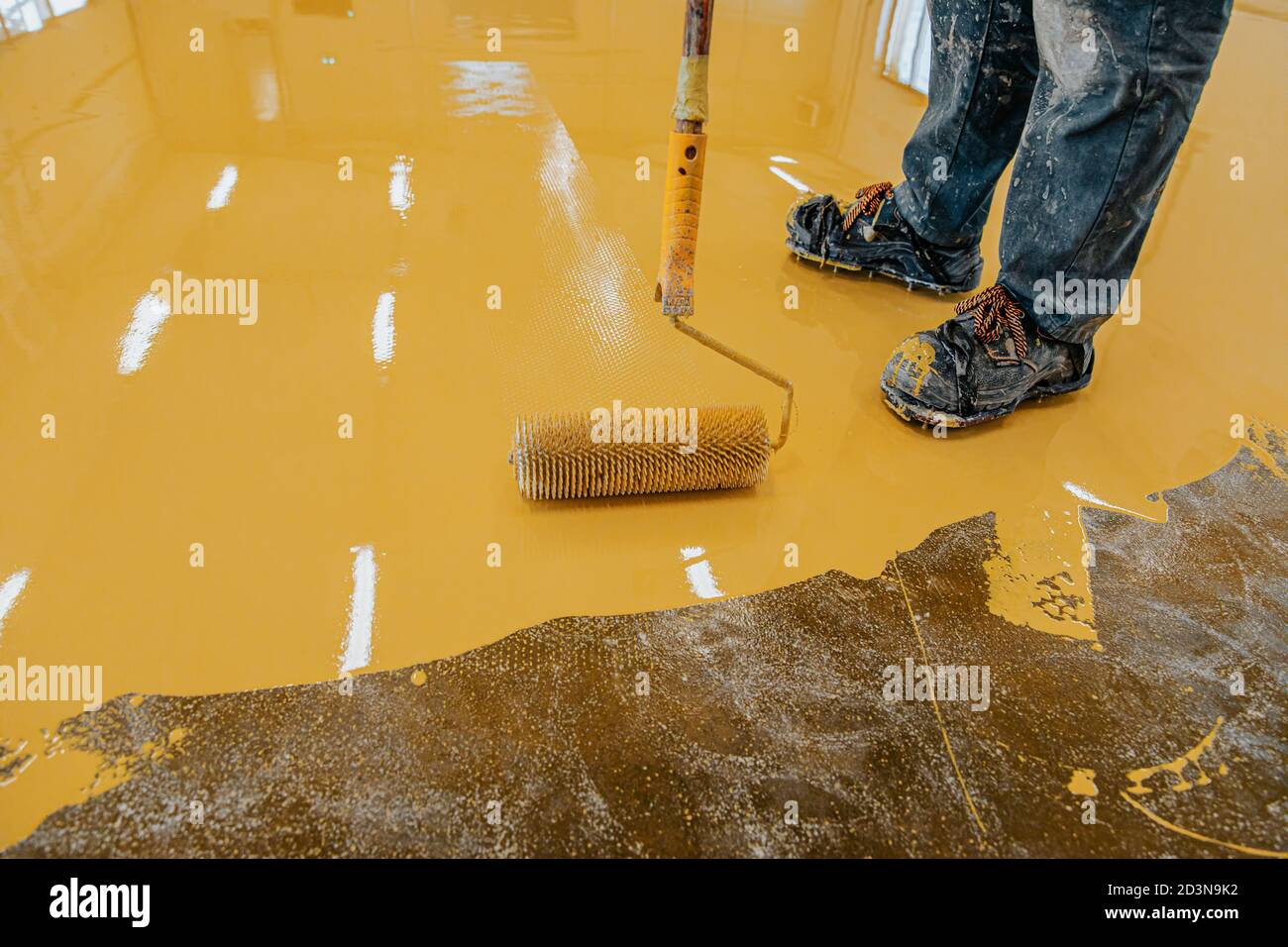 Worker, coating floor with self-leveling epoxy resin in industrial ...