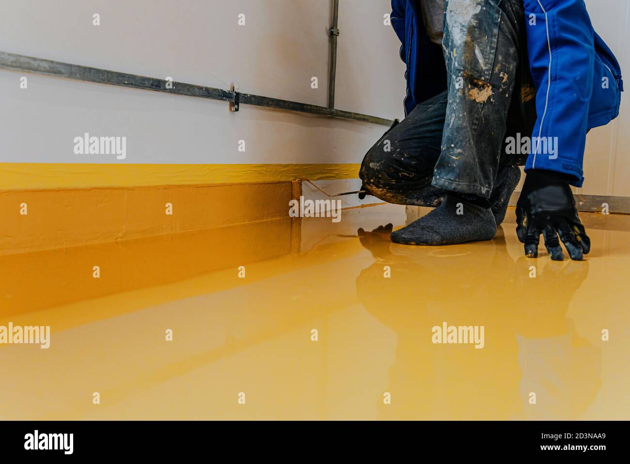Worker, coating floor with self-leveling epoxy resin in industrial ...