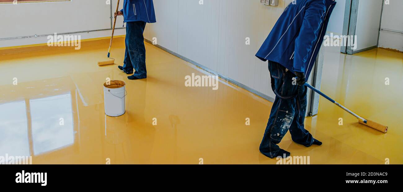Worker, coating floor with self-leveling epoxy resin in industrial ...