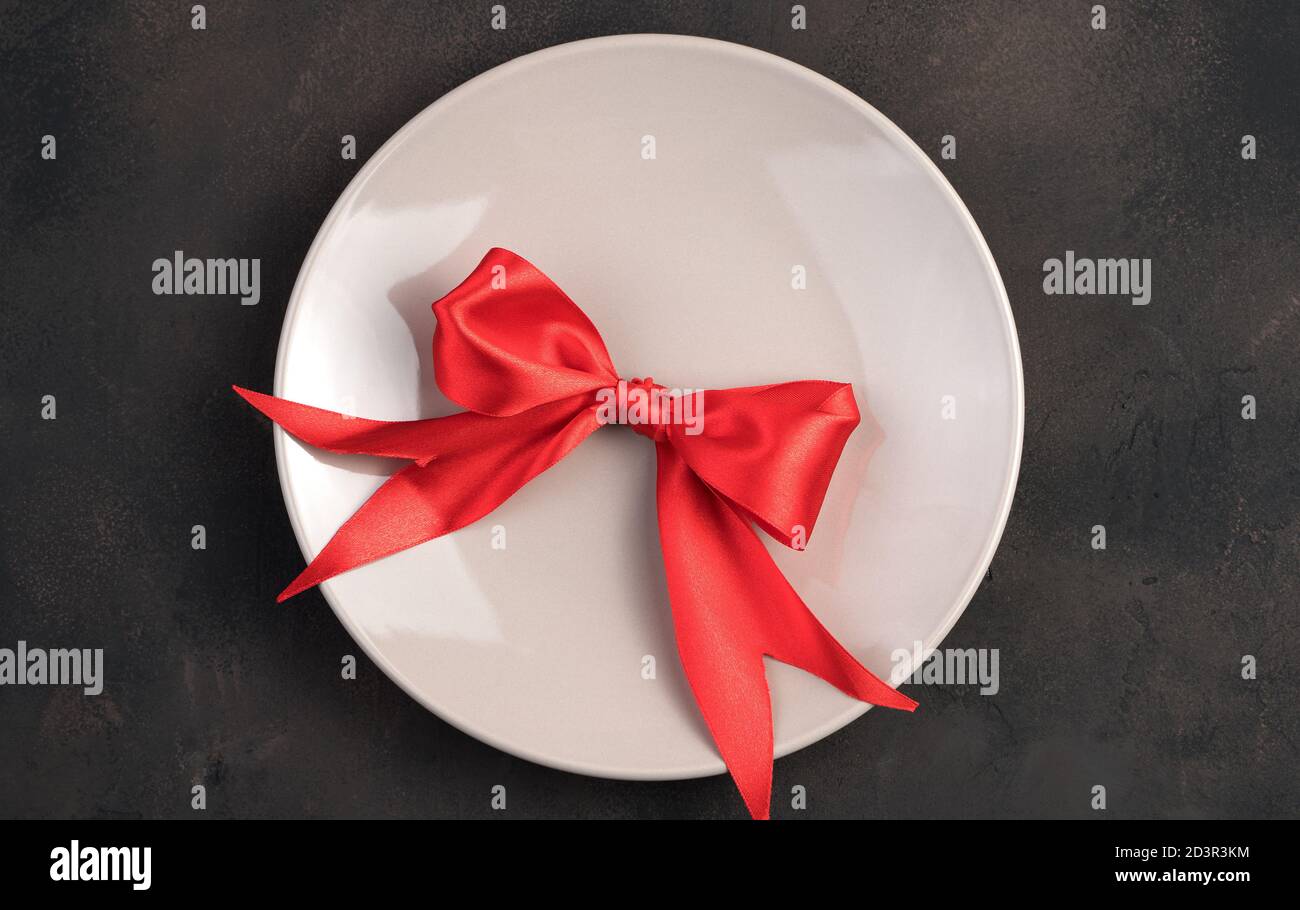 Red bow on a cream plate on a concrete brown background. The view from ...