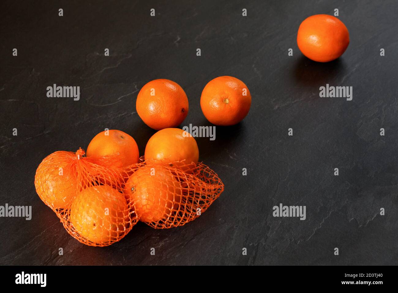 Oranges in red plastic net, some scattered on black stone like board ...