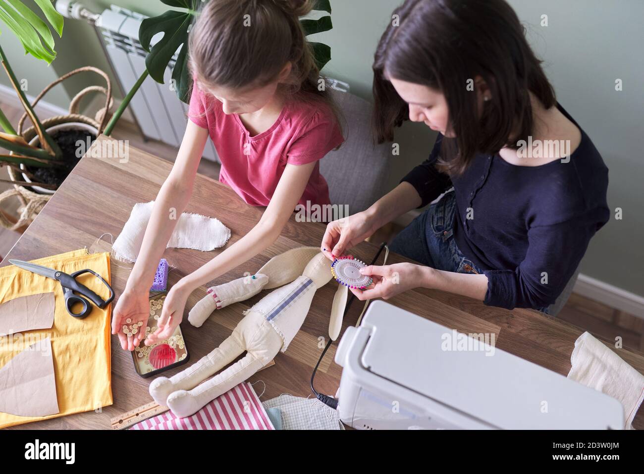 Family, two girls sisters teenager and younger together sewing toy doll ...